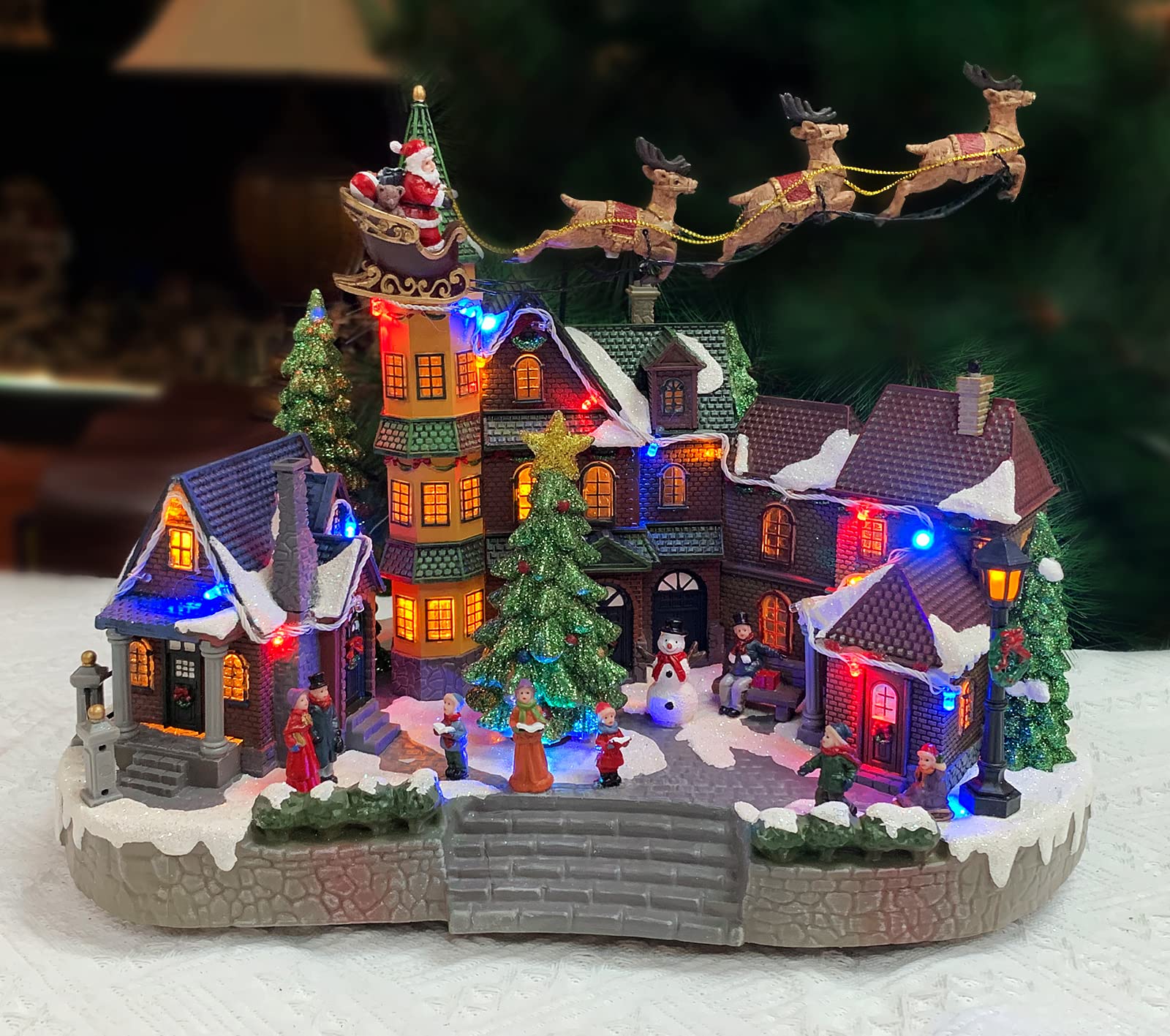 Christmas Village Centerpiece Decor, Santa Riding Sleigh Flying Over The Town Center, with Christmas Tree, featuring LED Lights, Christmas Music, and Animation - Power Adapter (included)