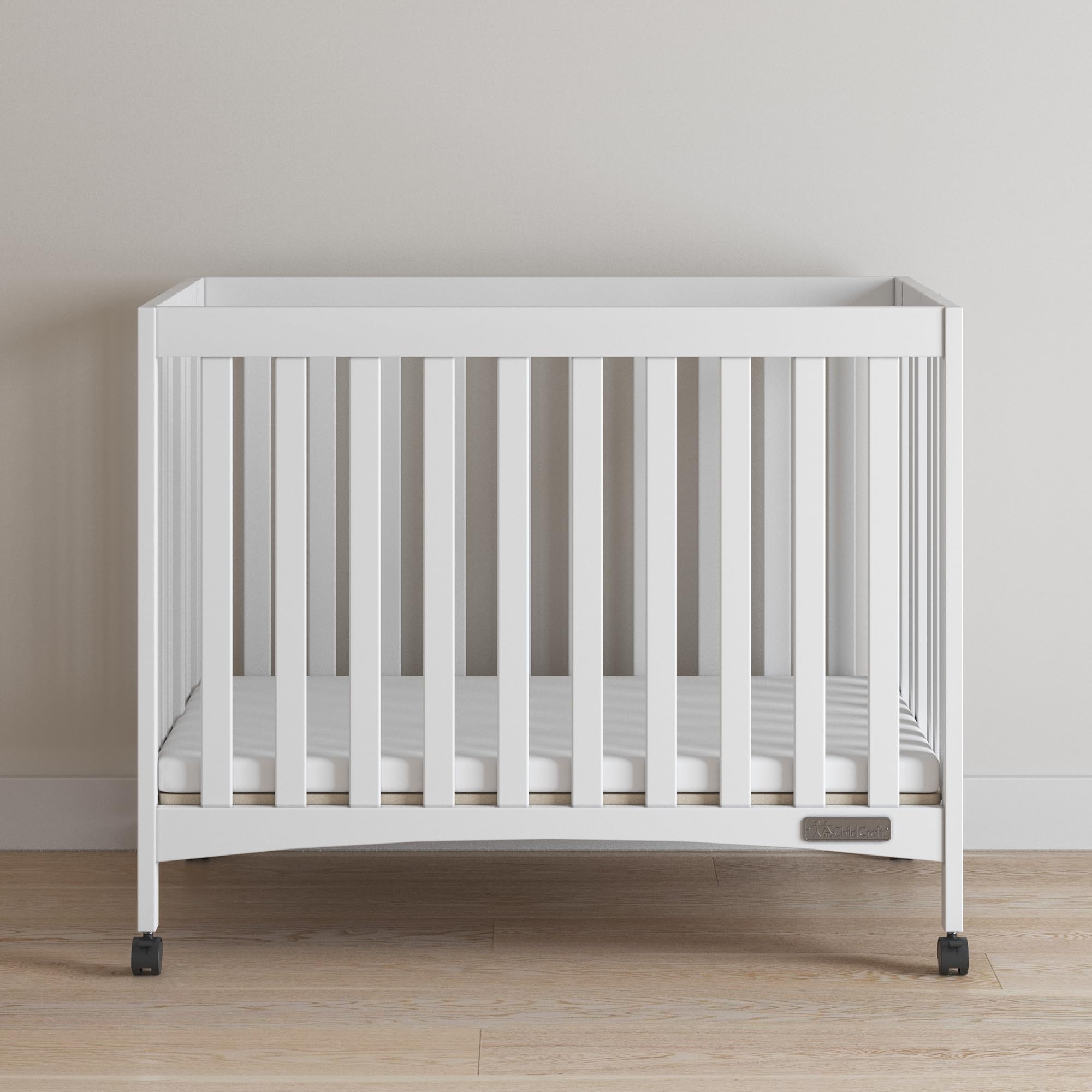 Child Craft London Mini Compact Folding Portable Crib with 2β Crib Mattress and 2 Easy Roll Locking Wheels, Durable Pine Wood Construction (Matte White)