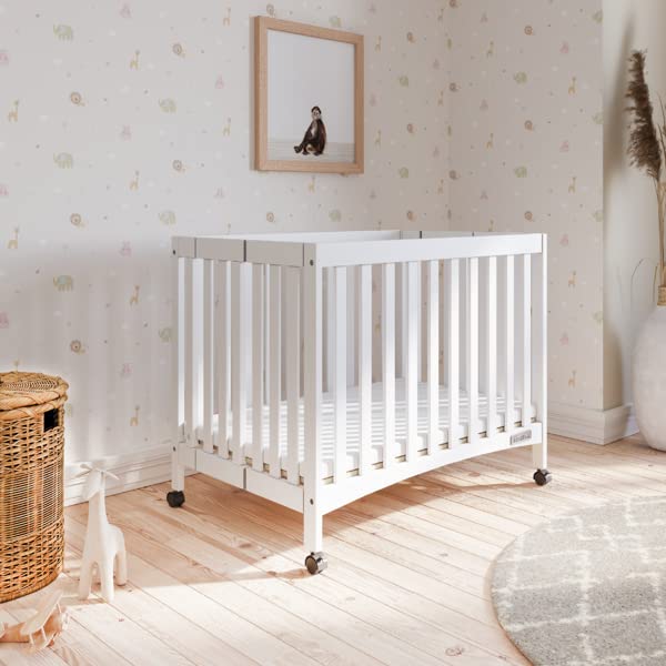 Child Craft London Mini Compact Folding Portable Crib with 2β Crib Mattress and 2 Easy Roll Locking Wheels, Durable Pine Wood Construction (Matte White)