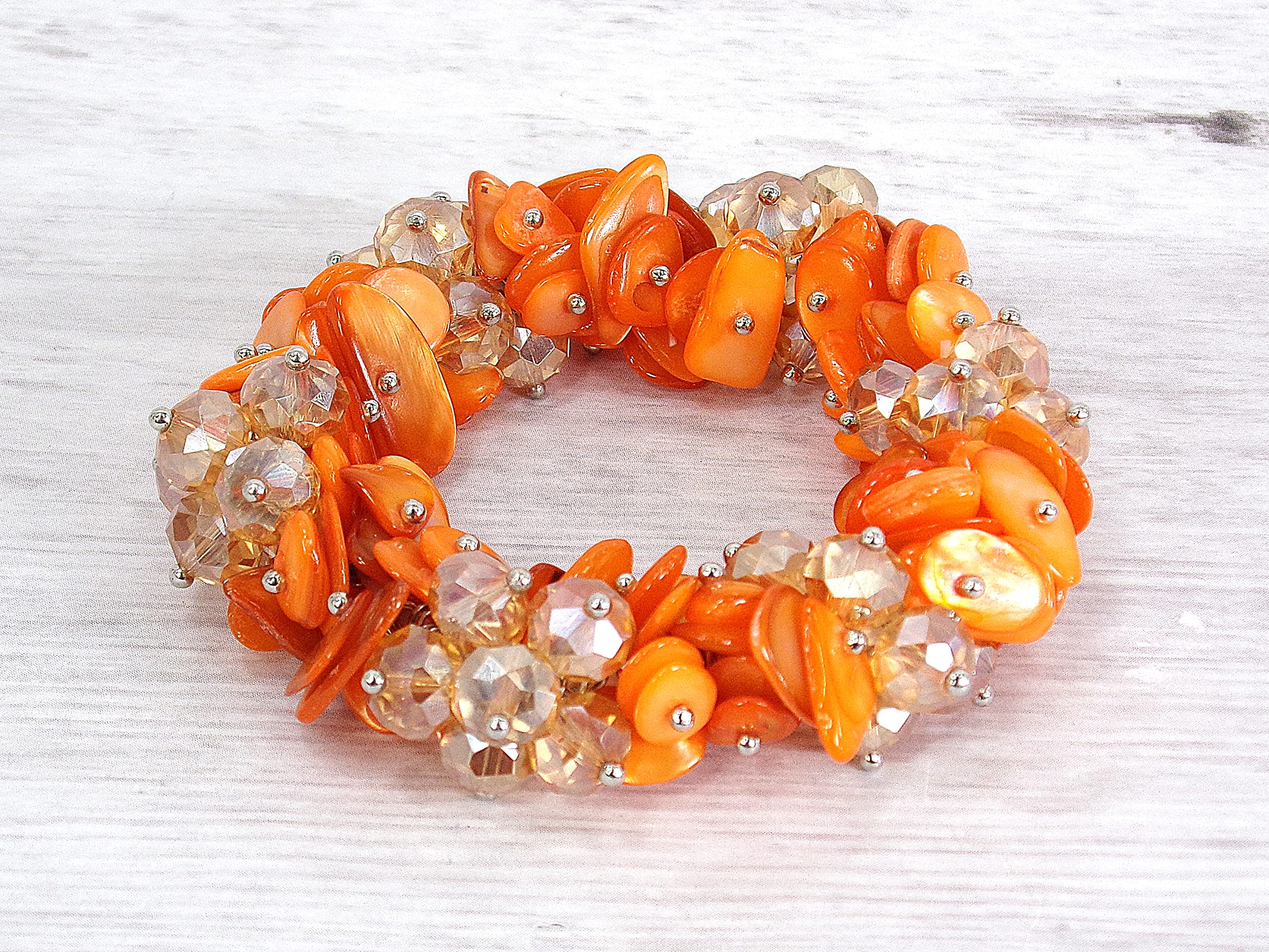 Calisa Designs Woman's orange shell and glass beaded stretch bracelet with silver beads, Designed with clusters of orange shell and orange facet cut glass beads.